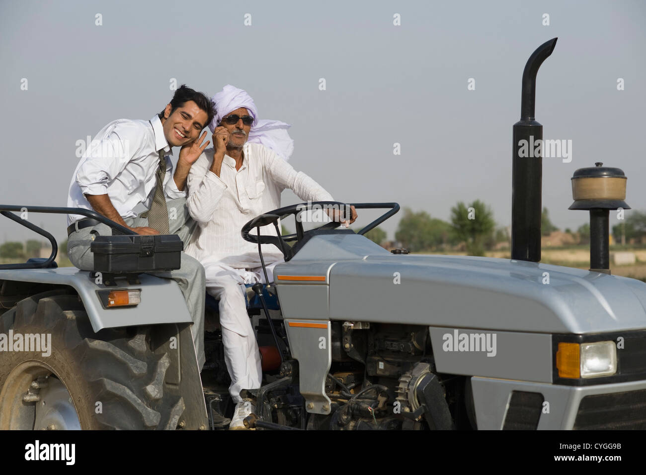 Farmer talking on a mobile phone while driving a tractor with his son ...