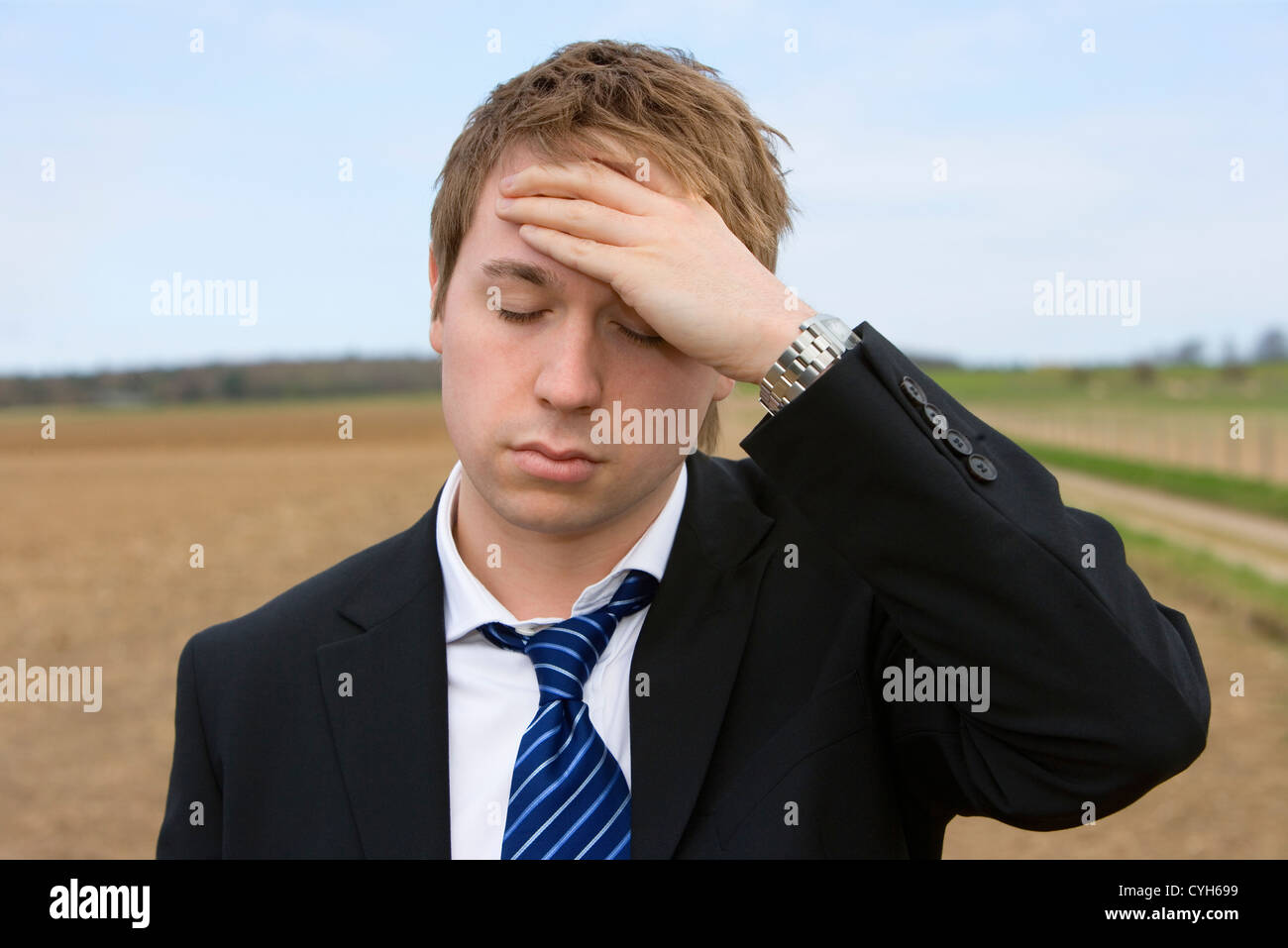 Young businessman with hand on forehead, standing in field Stock Photo ...