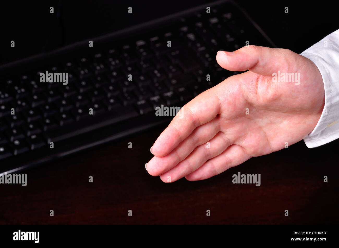 Hand ready for an handshake next do a computer keyboard on a dark table ...