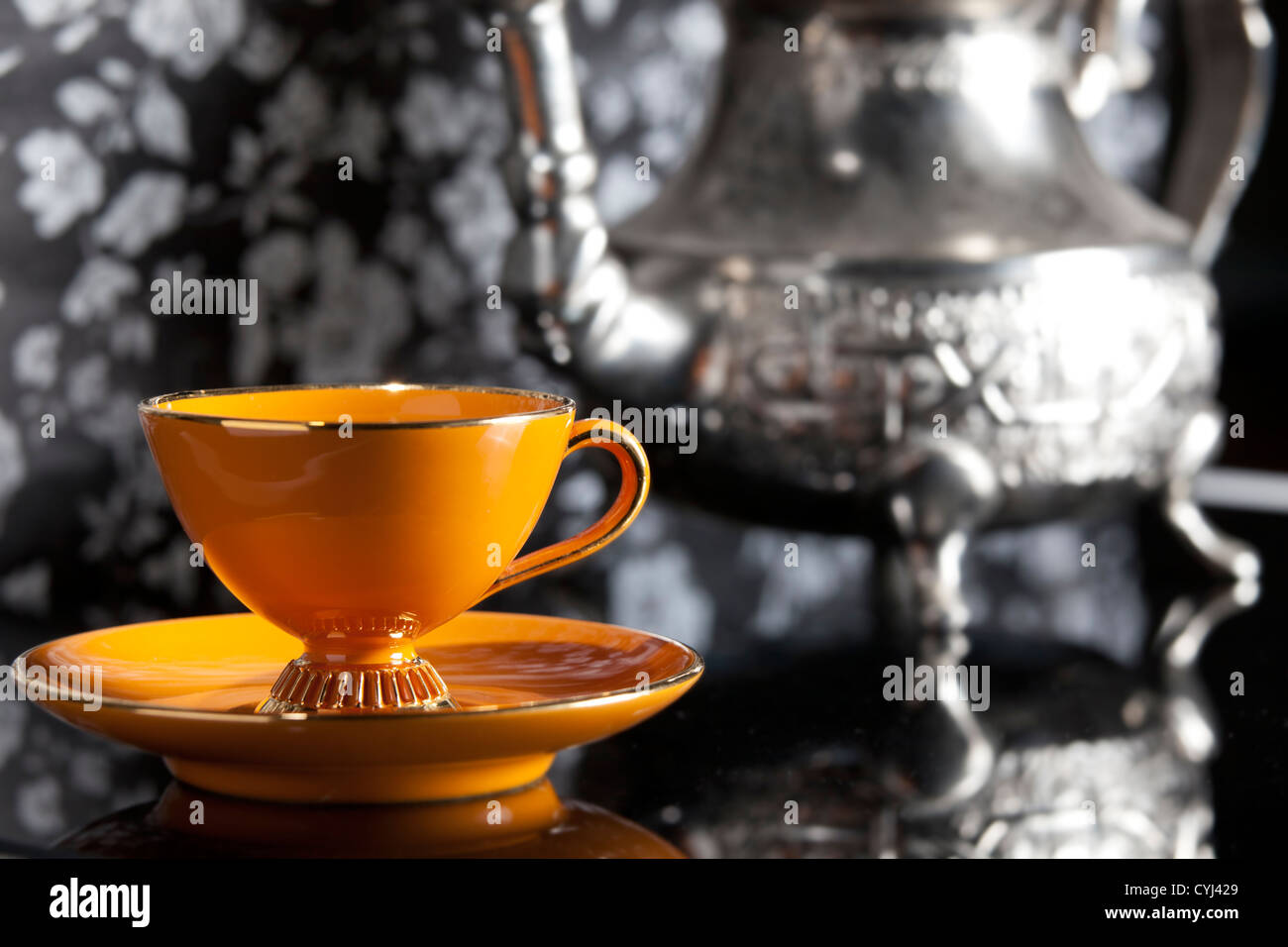 Tea cup and silver teapot with reflection and bold orange teacup with ...
