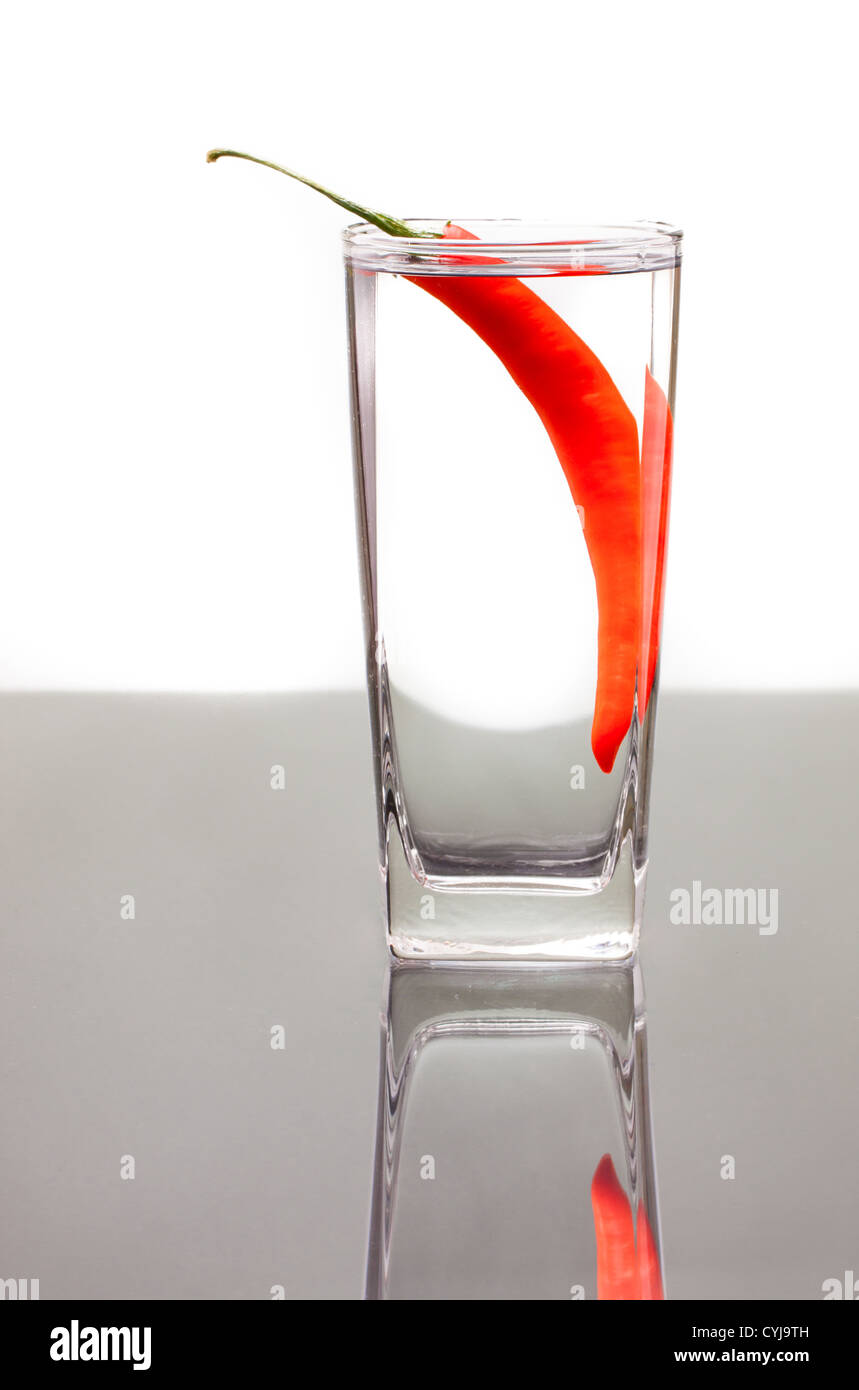 A clear alcoholic drink with a red chilli pepper. On table with ...