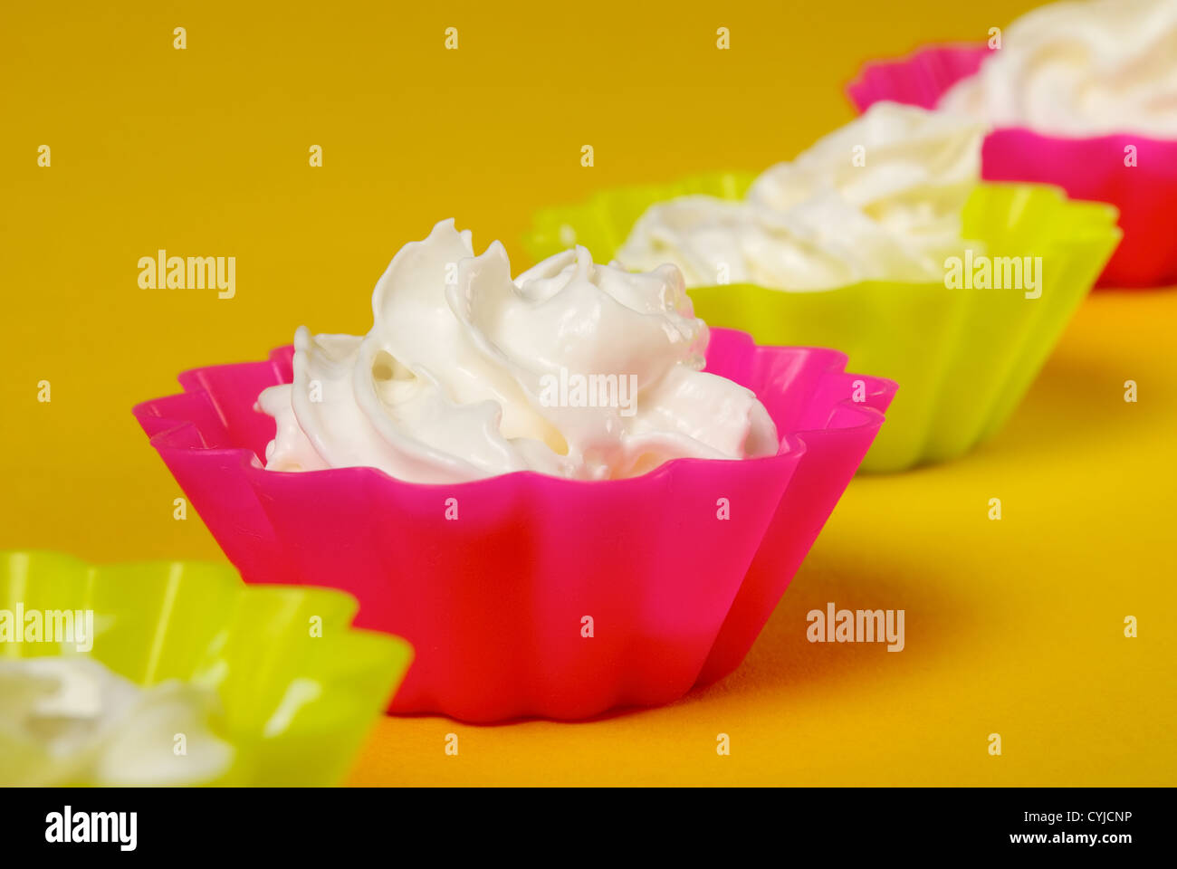 Four portions of whipped cream over yellow background. Shallow DOF├ô ...