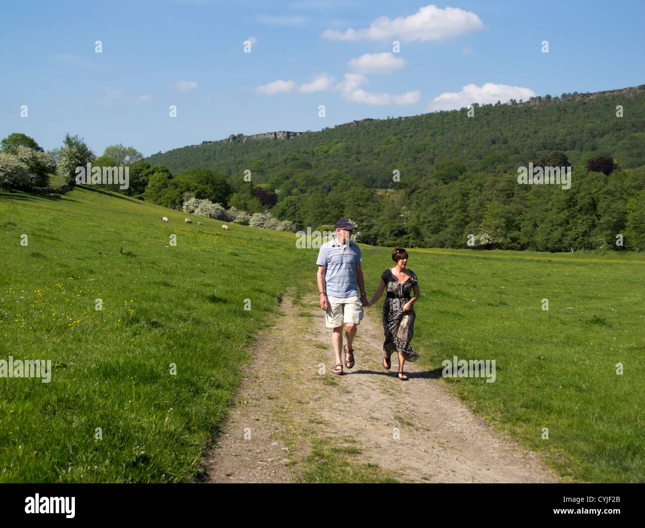 Man and woman walking together along path in field holding hands ...