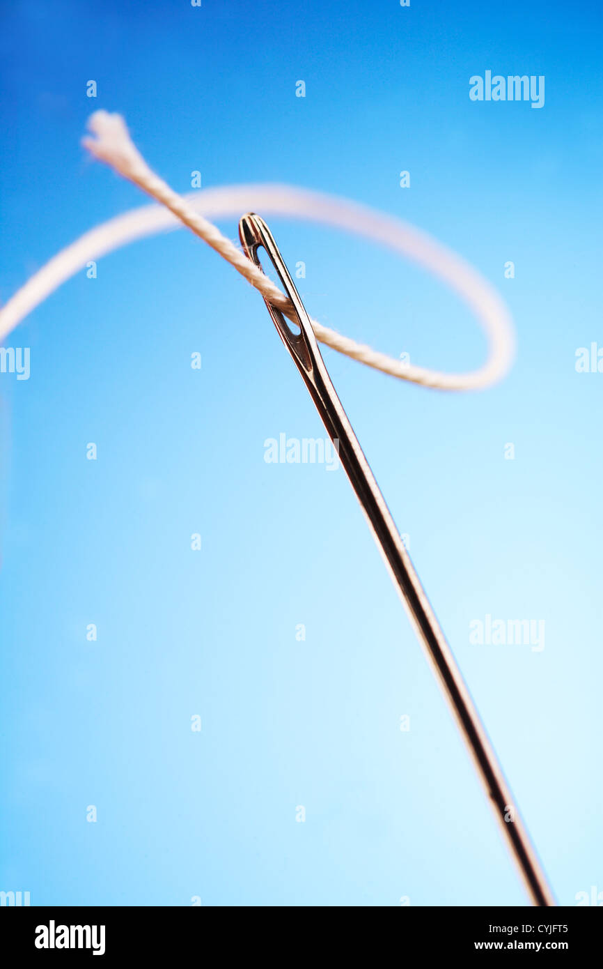 Thread passing through needle eye, close-up on blue background Stock ...