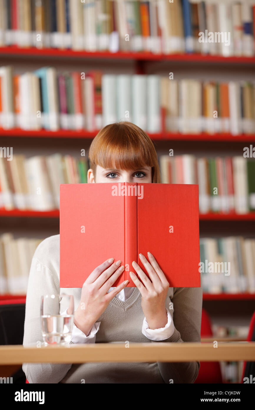 Girl hiding behind the book on library Stock Photo - Alamy