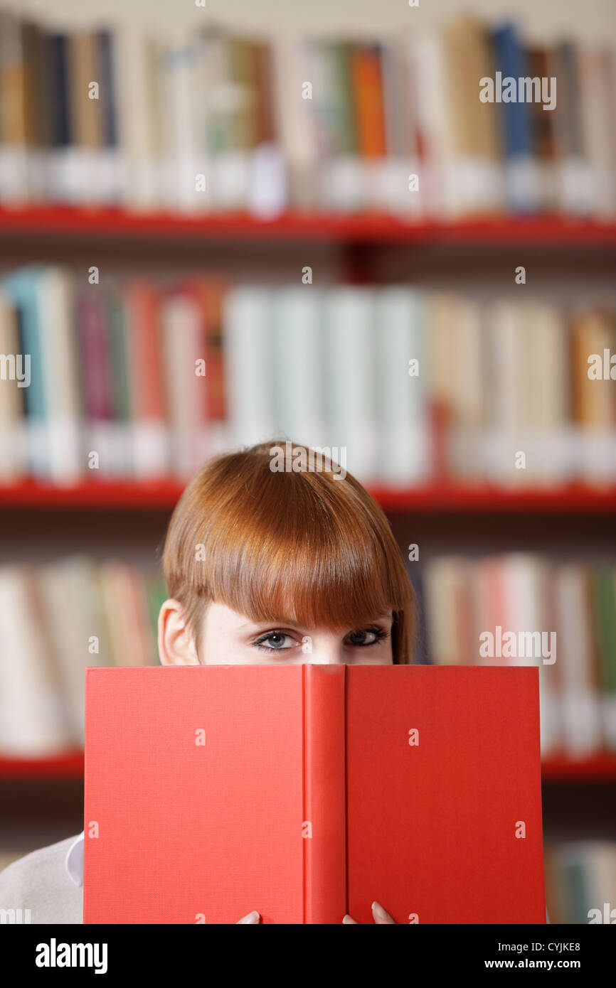 Girl hiding behind the book, library on background Stock Photo - Alamy