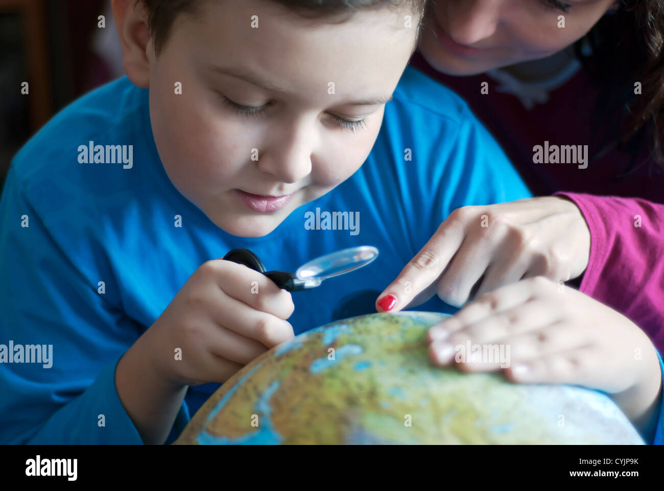 Concentrated boy sitting and searching something at globe with his ...