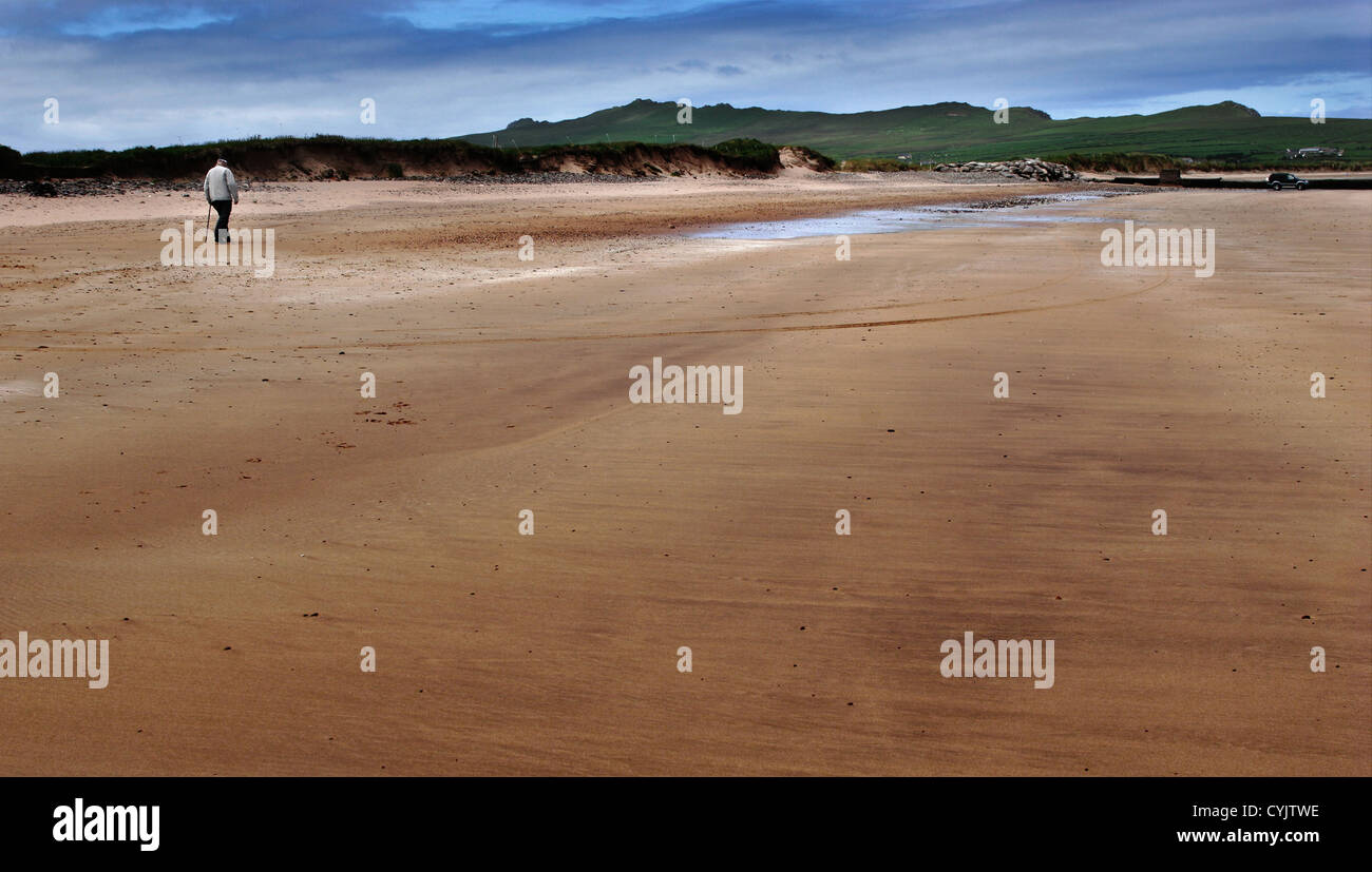 An old man walking along the sandy beach of Ballyferriter, County Kerry ...