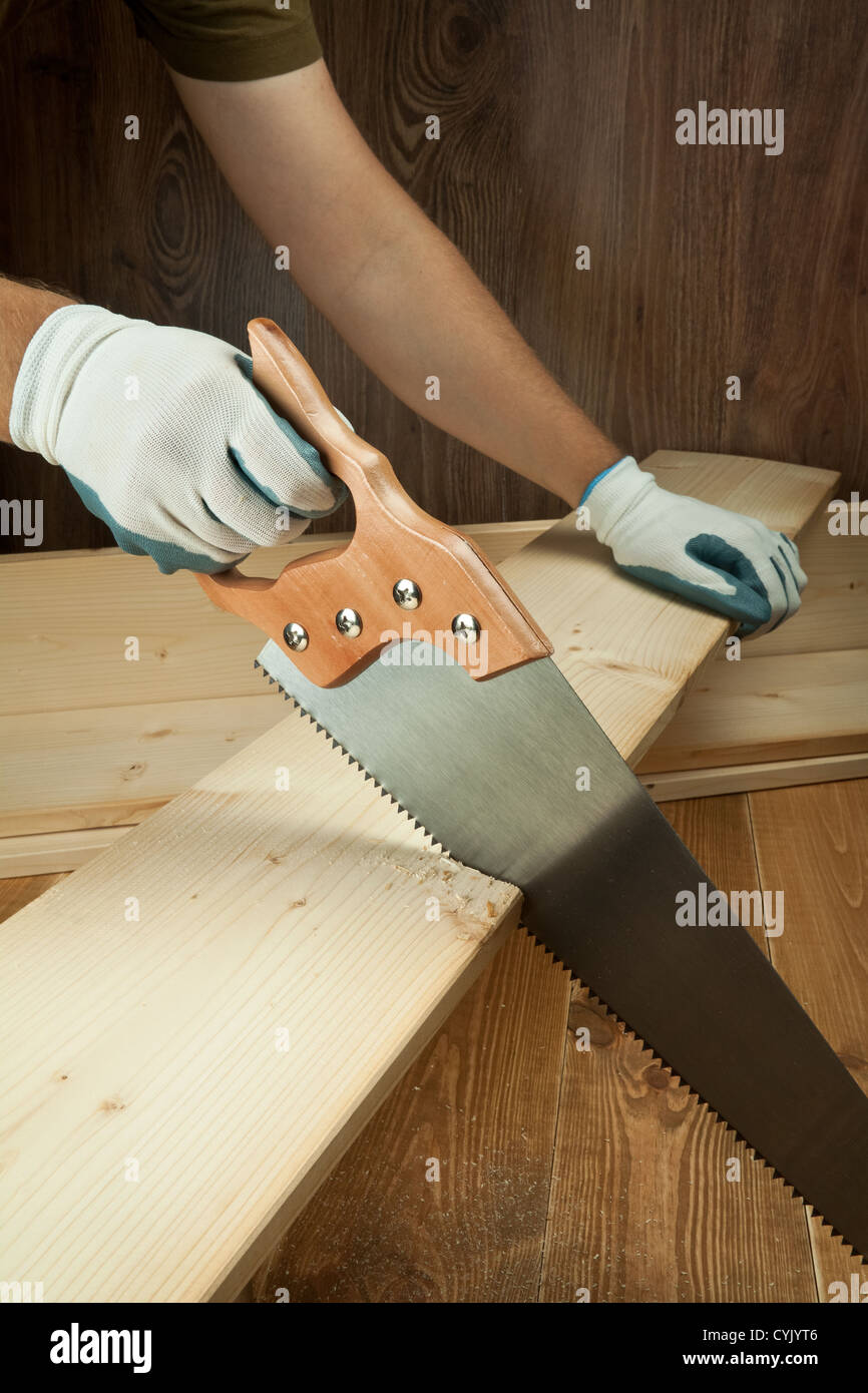 Wood workshop. Carpenter cutting plank with hand saw Stock Photo - Alamy