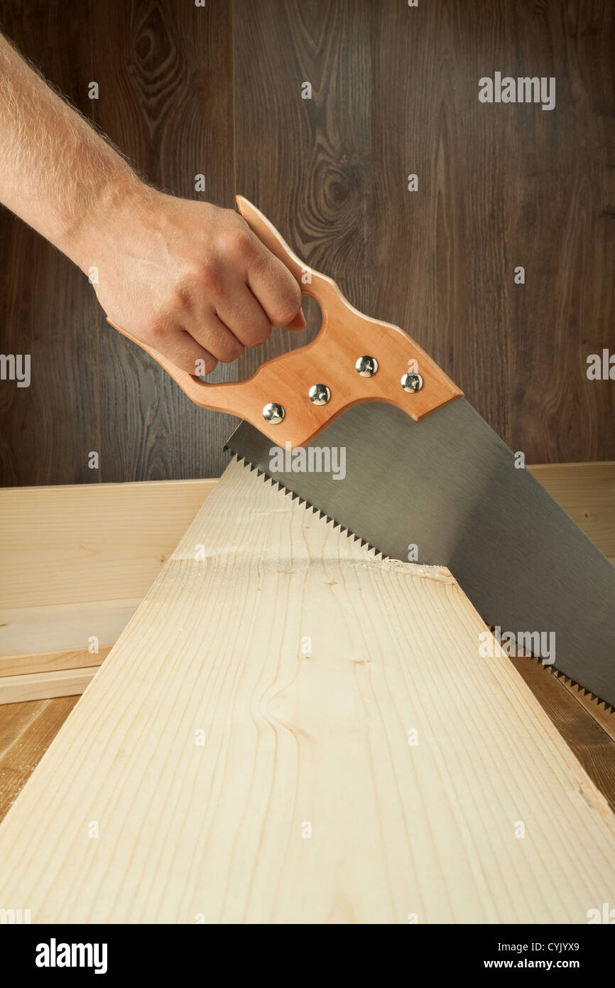 Wood workshop. Carpenter cutting plank with hand saw Stock Photo - Alamy