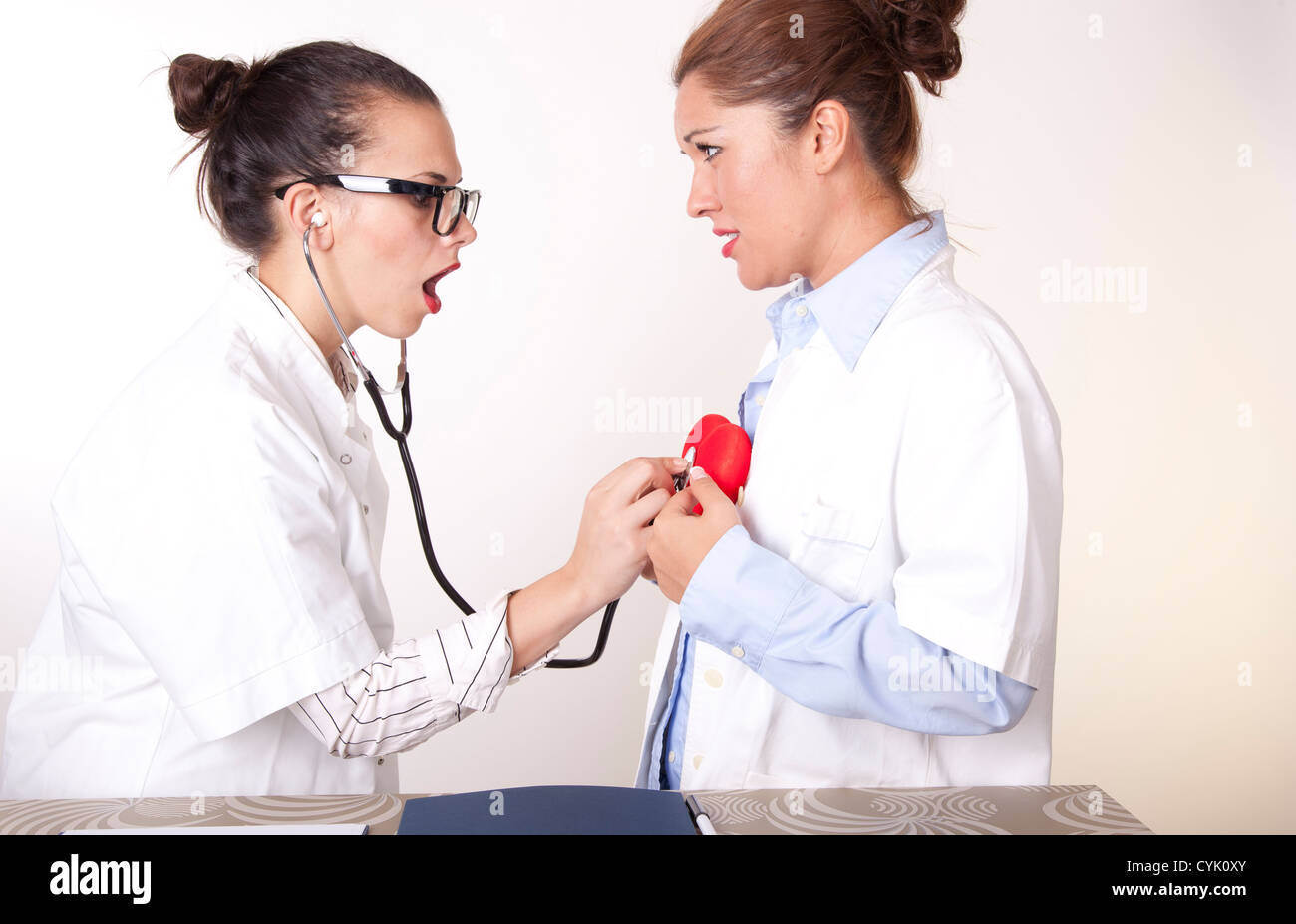 Portrait of a two young beautiful female doctors checking a red heart ...