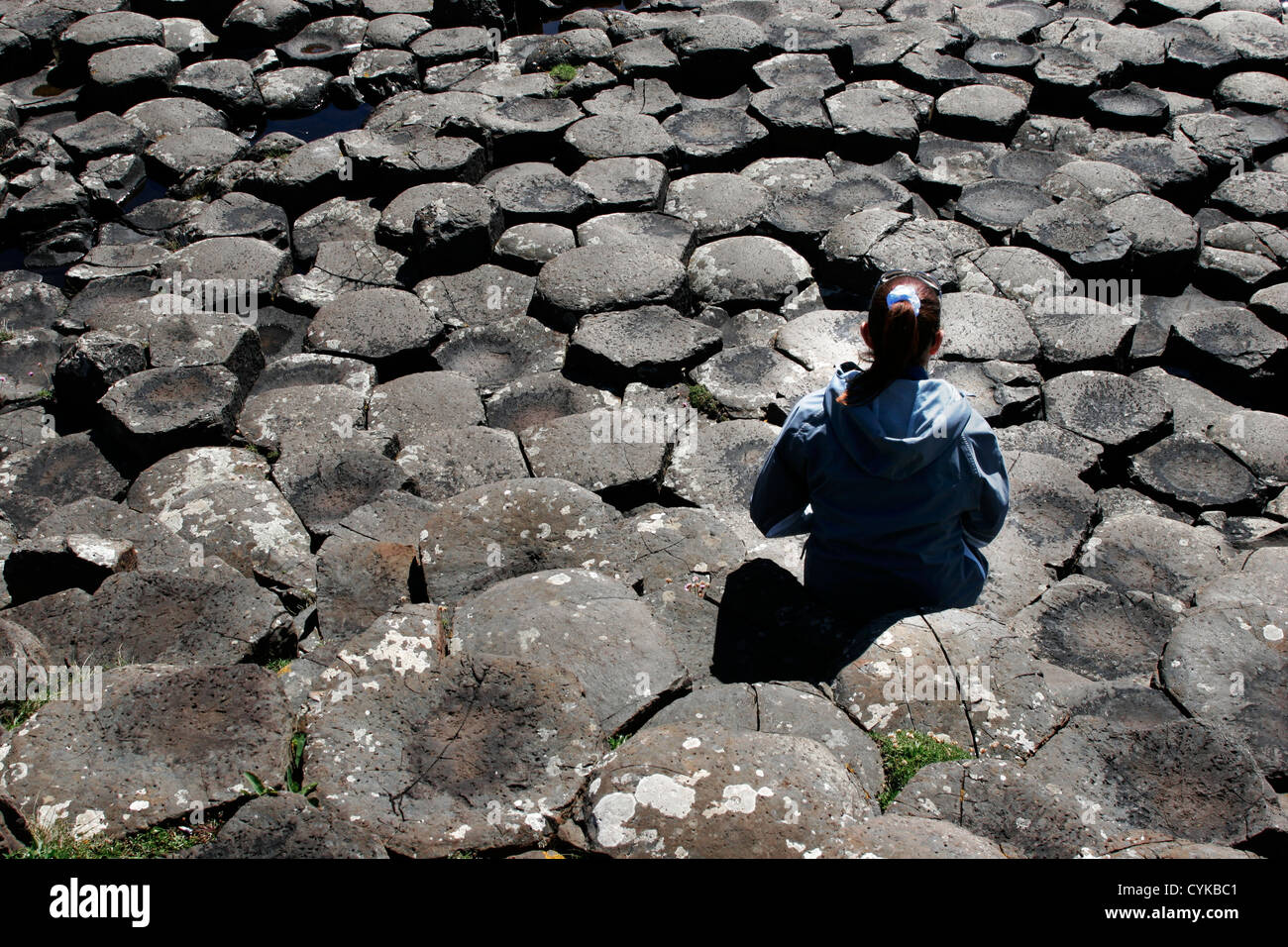 A woman is seated on one of the polygonal basalt columns of the Giant's ...