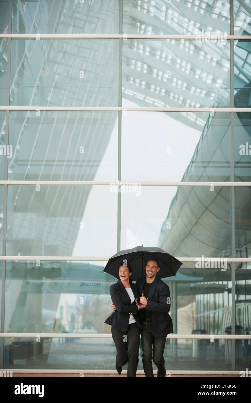 Caucasian business people running together underneath umbrella Stock ...