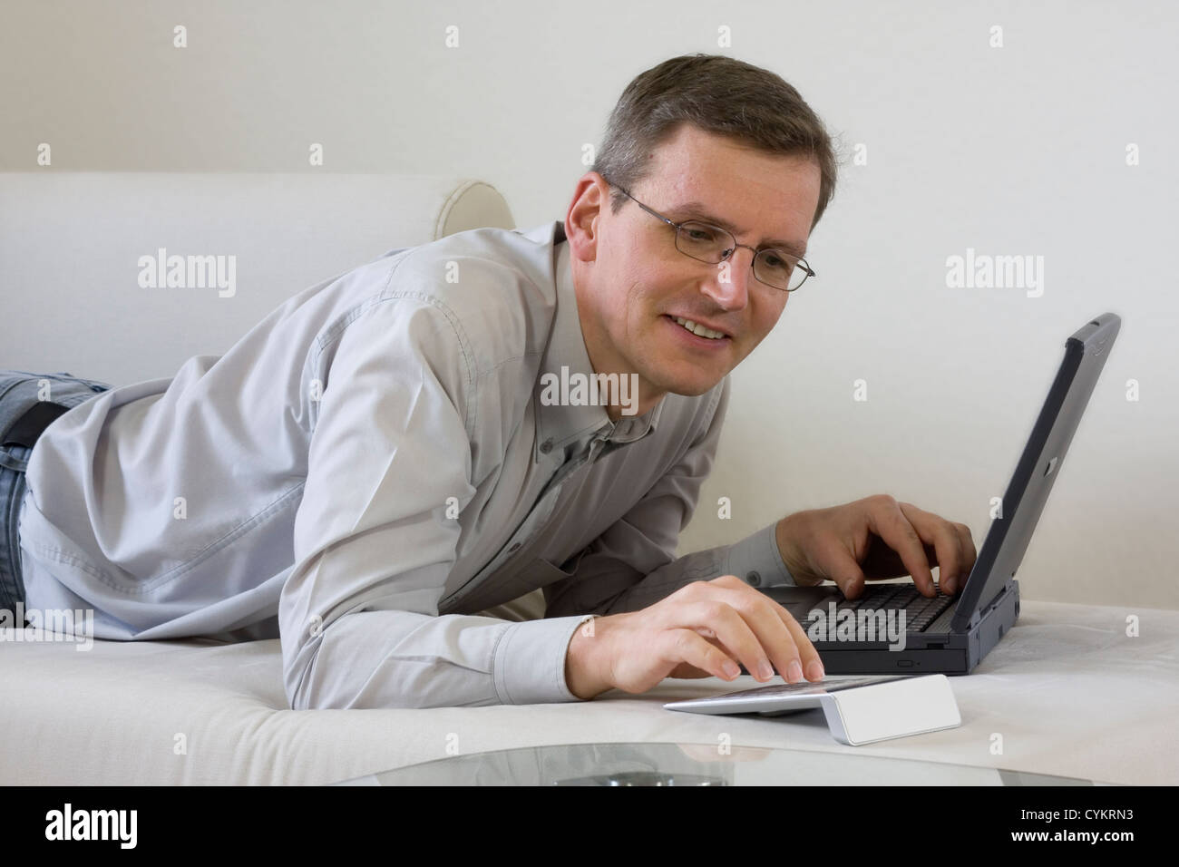 Man lying on a coach with laptop computer and calculator Stock Photo ...