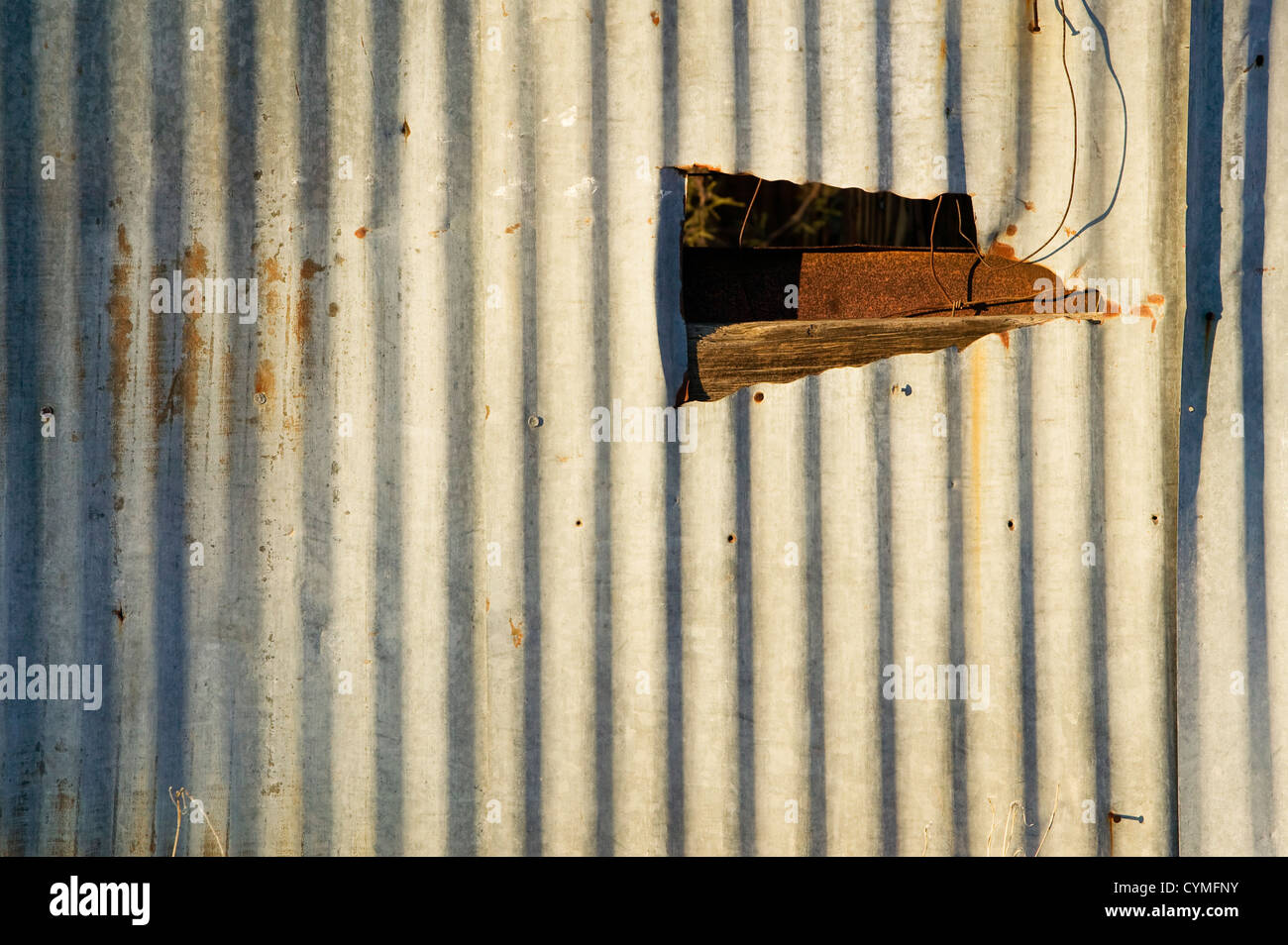 Rusty corrugated metal with a late-day shadow and a ragged hole Stock ...