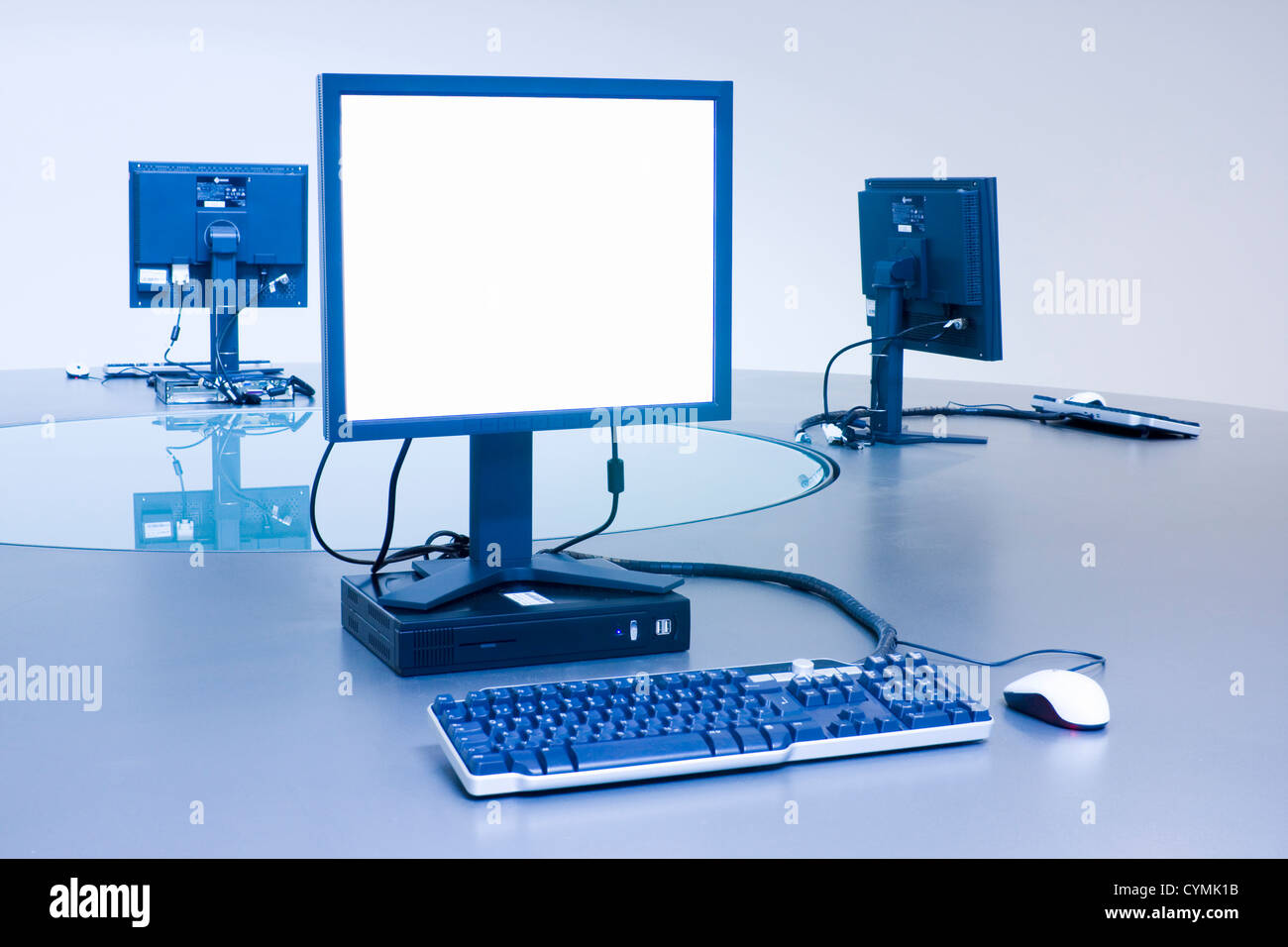 Three computers with keyboards on a big round table Stock Photo - Alamy