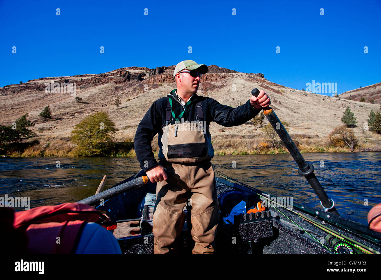 A fisherman guides a dory boat on the Deschutes River with mountains in ...