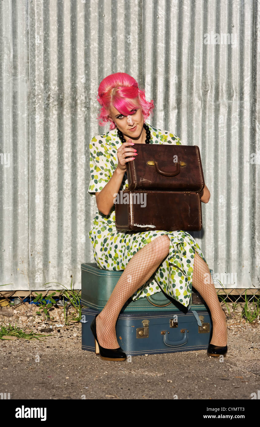Woman with pink hair wearing polka dot dress in alley with suitcases ...
