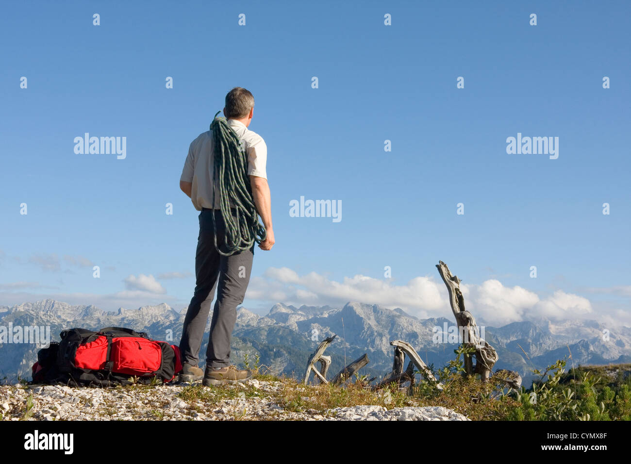 Mountaineer with rope on mountain peak contemplating the landscape ...