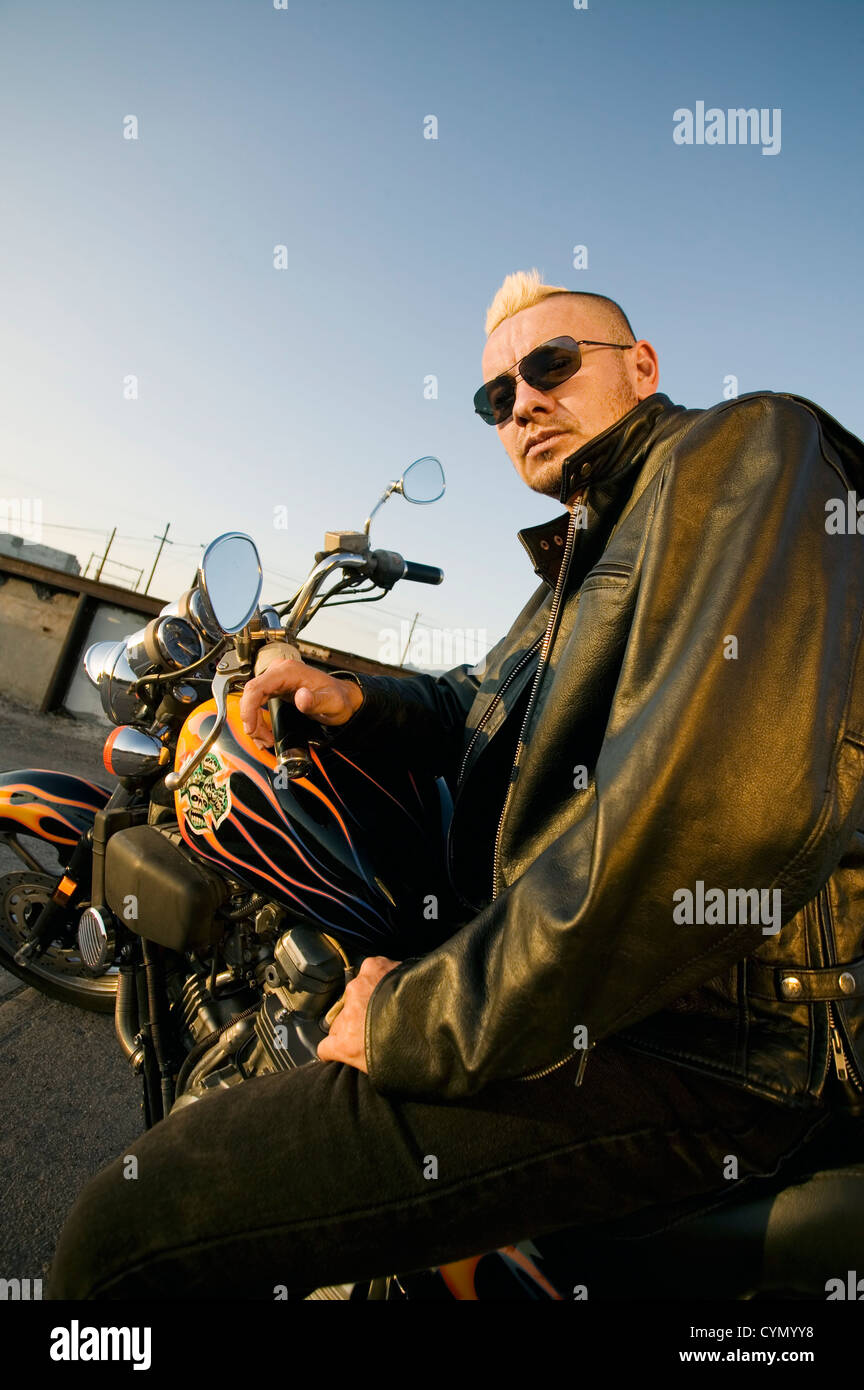 Man with a punk haircut in a leather jacket sitting on his motorcycle ...
