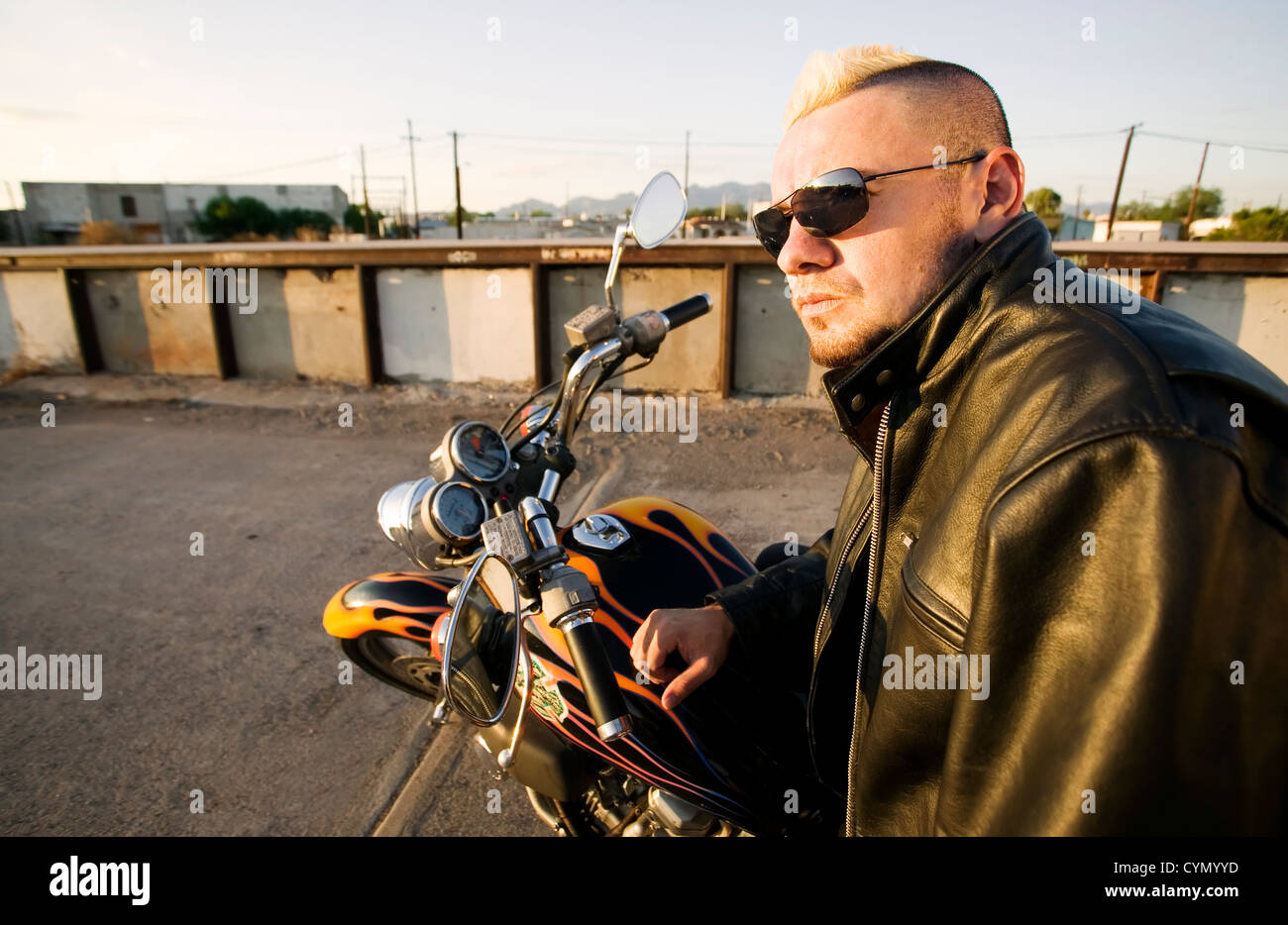Man with a punk haircut in a leather jacket sitting on his motorcycle ...