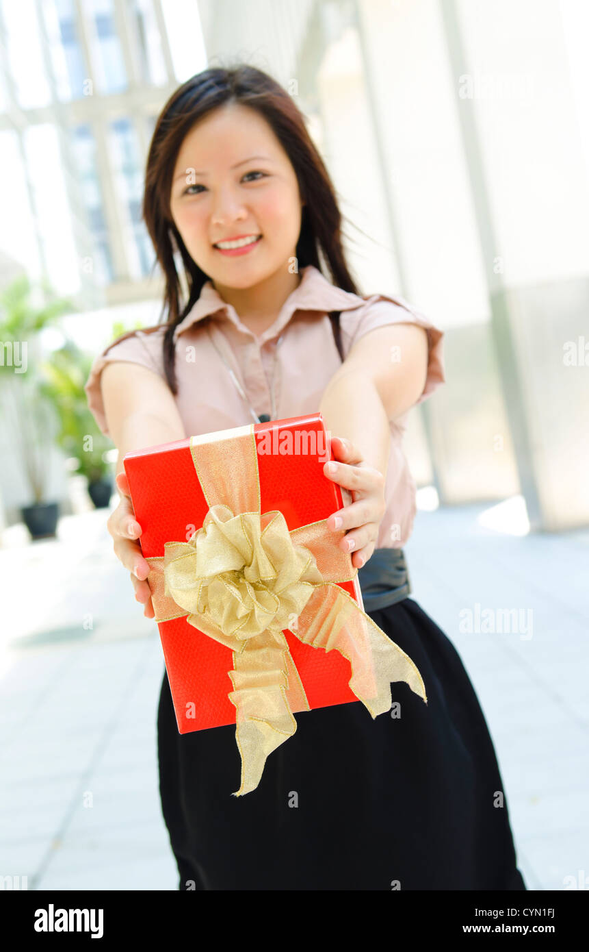 Young Asian girl arms out holding a beautiful wrapped present. Focus is ...