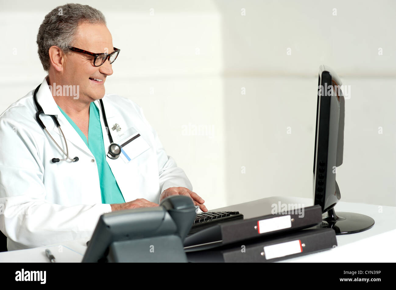 Experienced smiling male doctor working on computer, typing on keyboard ...