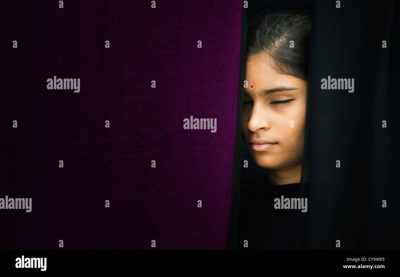 Indian girls face with eyes closed standing between dark shawls. India ...