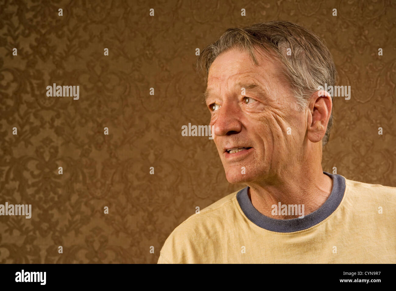 Man with a craggy face wearing a yellow shirt against a gold background ...