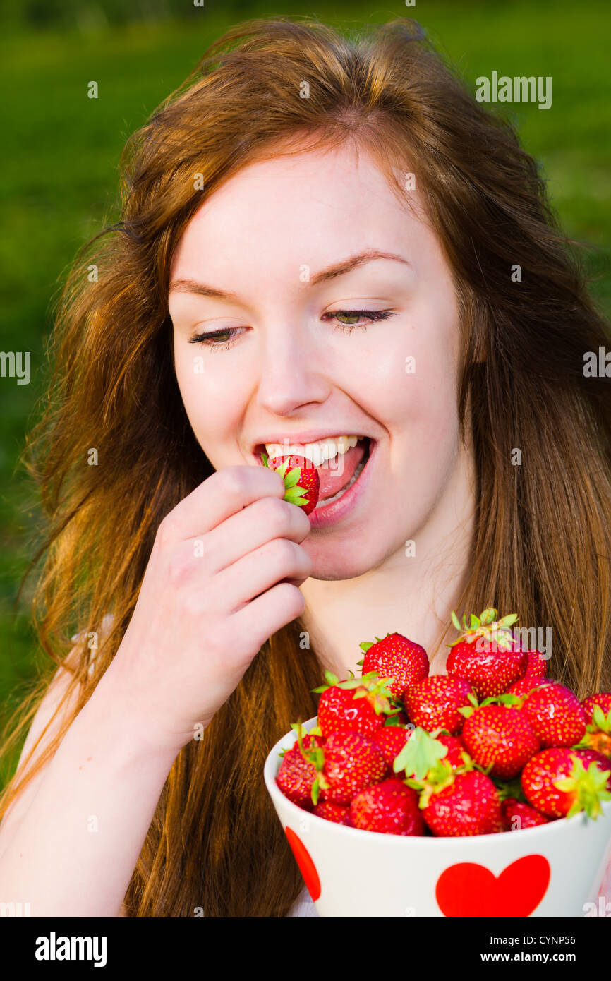 Beautiful girl taste a strawberry, full bowl of berries, focus on the ...