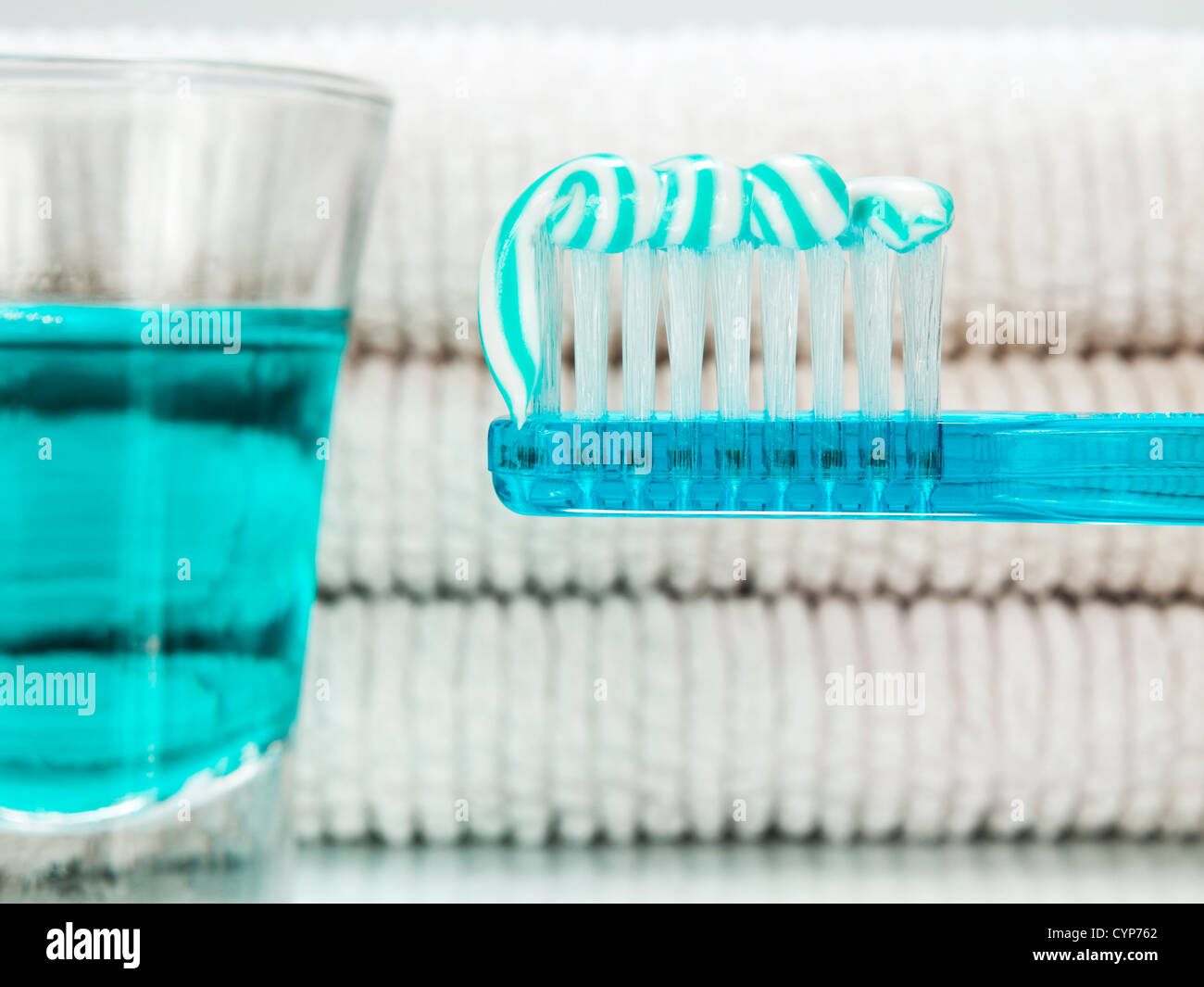 A blue toothbrush with toothpaste, a glass full of mouthwash and towels ...