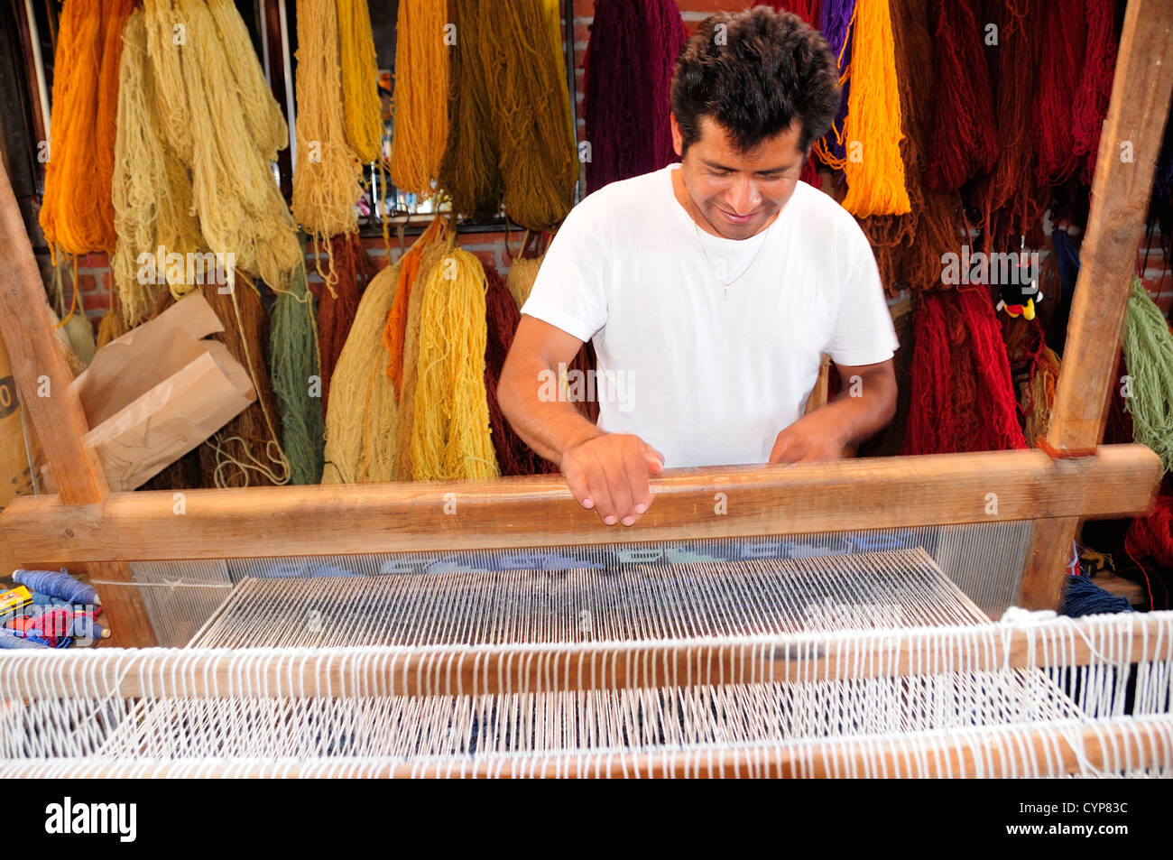 Weaver at loom with different coloured yarn hanging in bundles behind ...