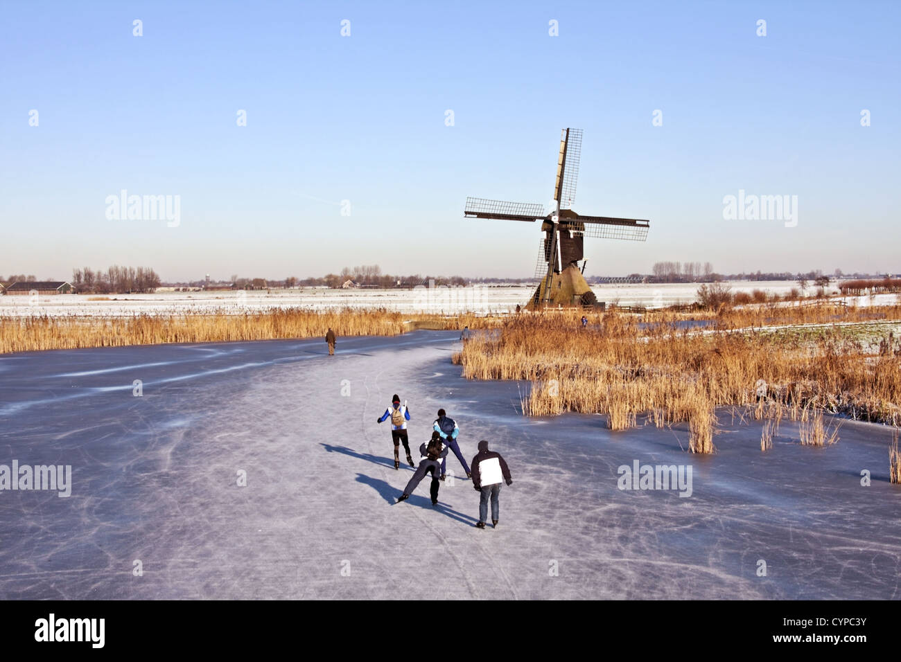Typically dutch: ice skating on a frozen lake with view on a windmill ...