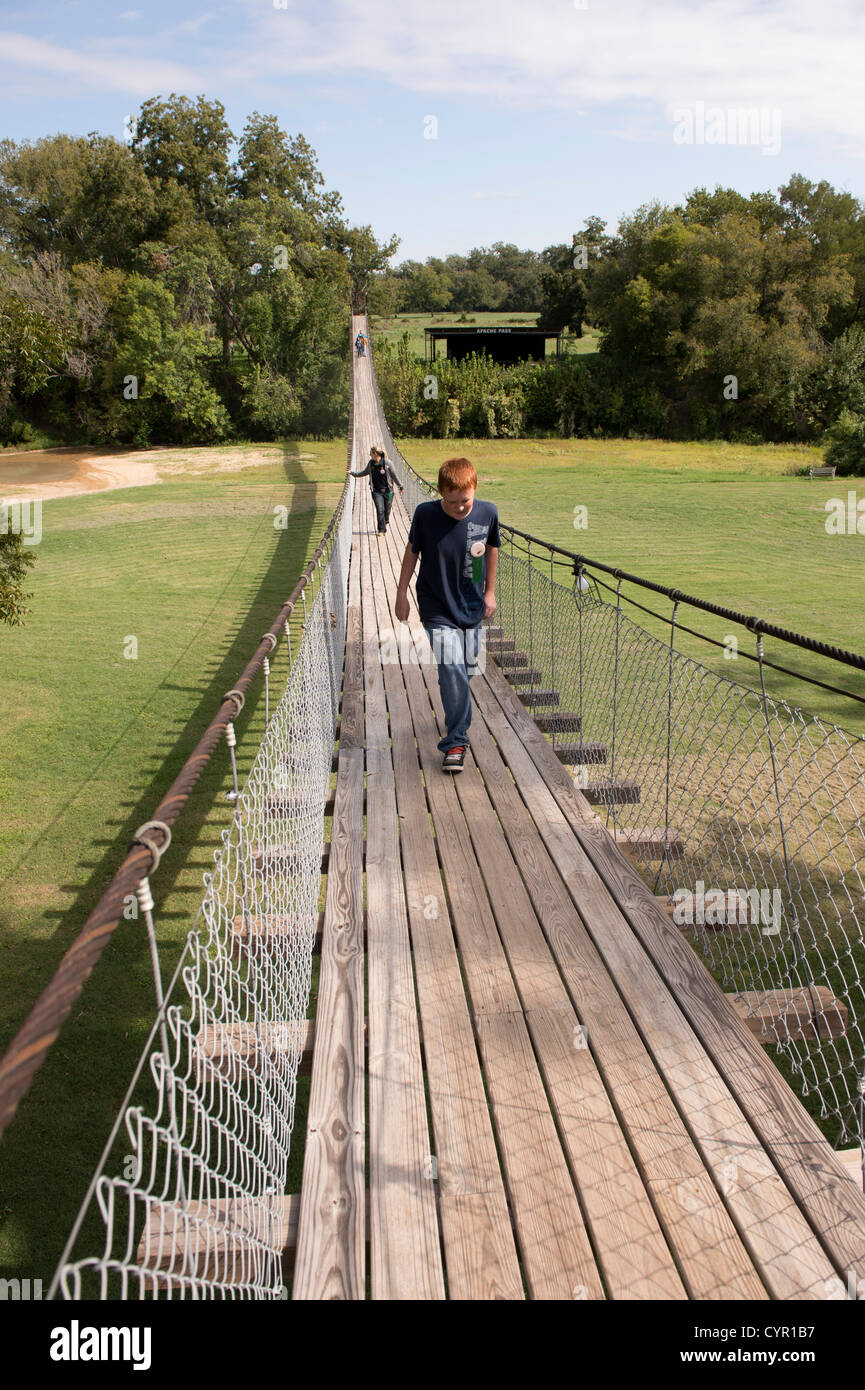 Junior high school students walk across a wood-plank swinging bridge ...