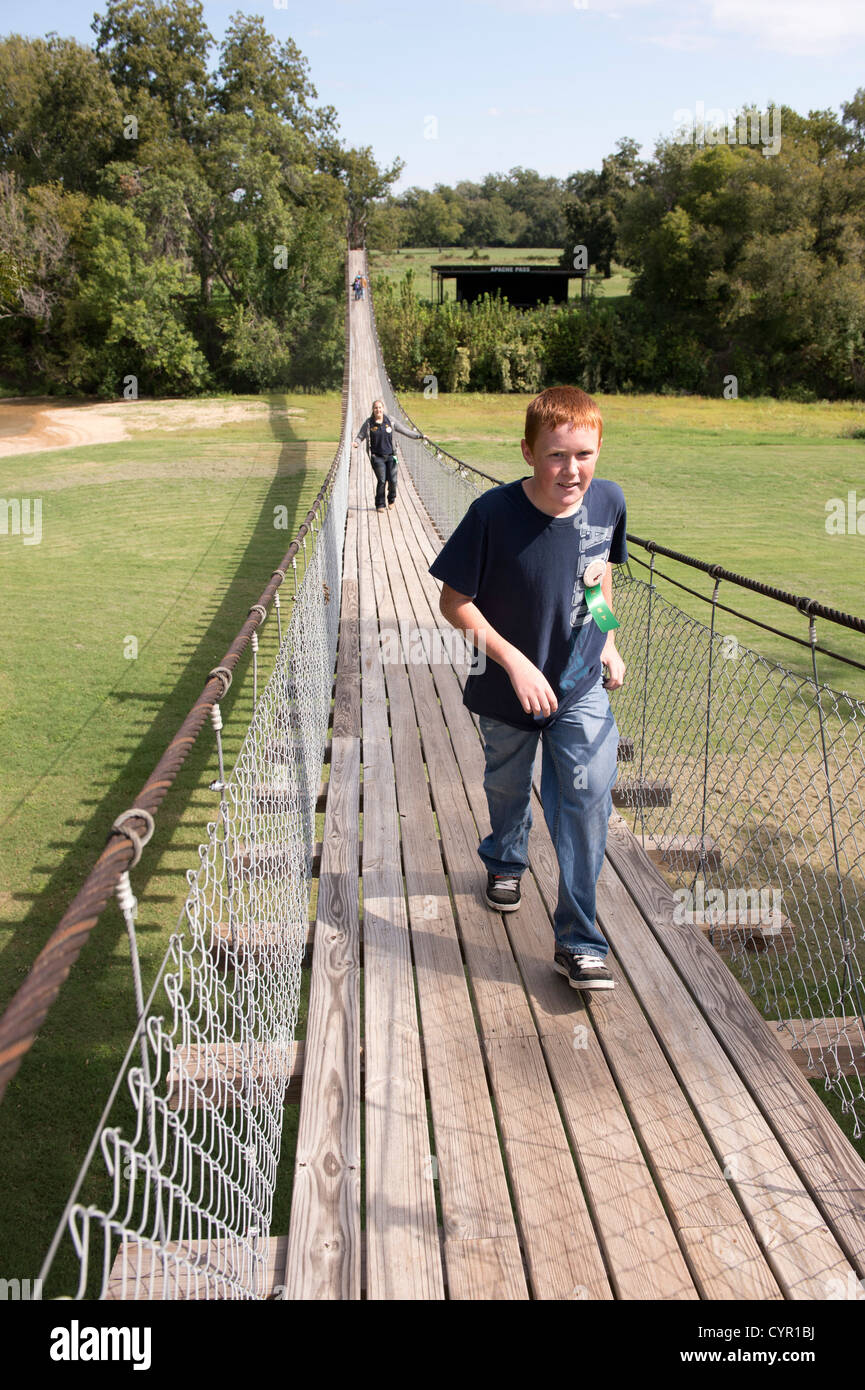 Junior high school students walk across a wood-plank swinging bridge ...