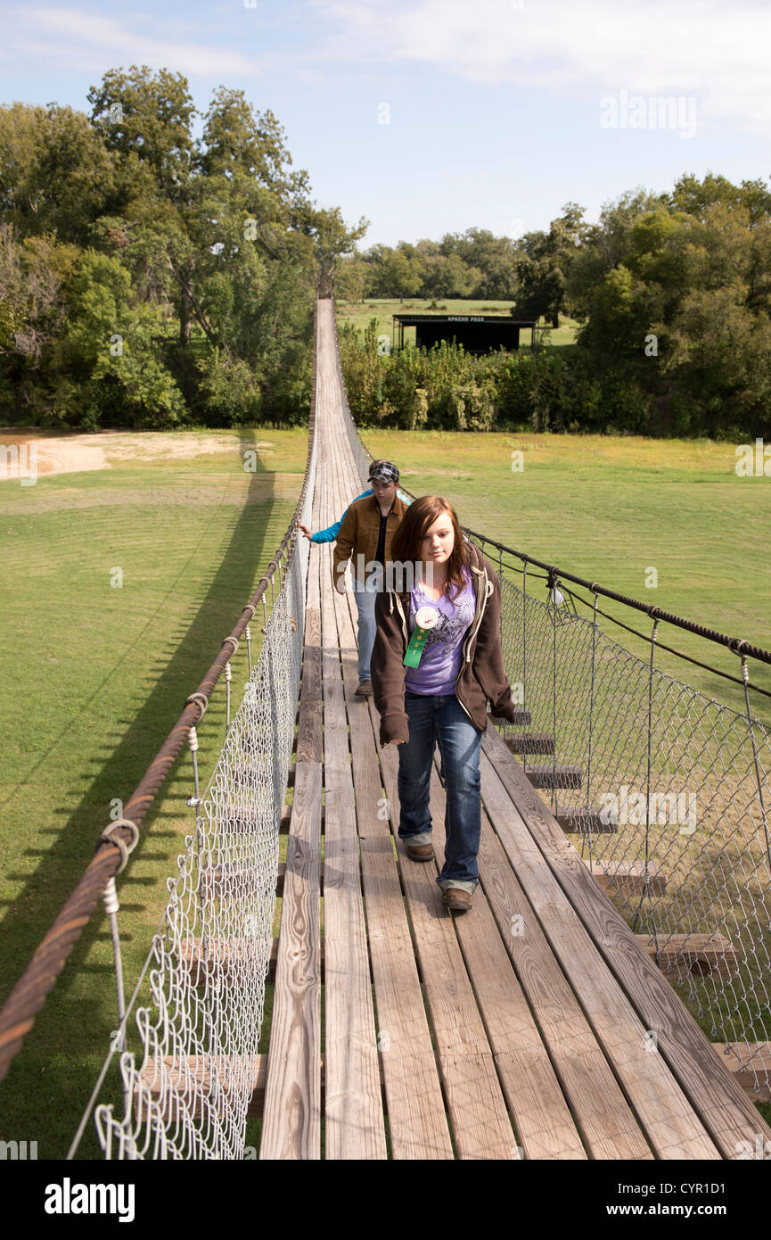 Junior high school students walk across a wood-plank swinging bridge ...
