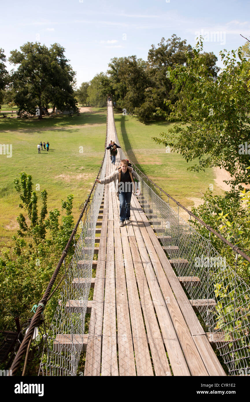 Junior high school students walk across a wood-plank swinging bridge ...