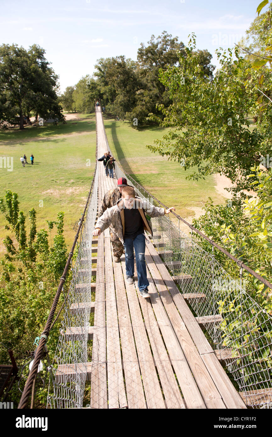 Junior high school students walk across a wood-plank swinging bridge ...
