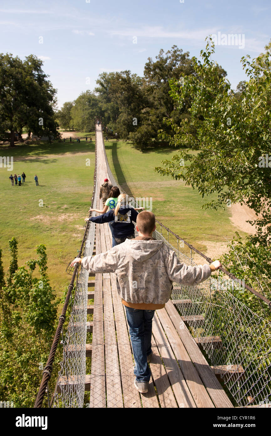 Junior high school students walk across a wood-plank swinging bridge ...