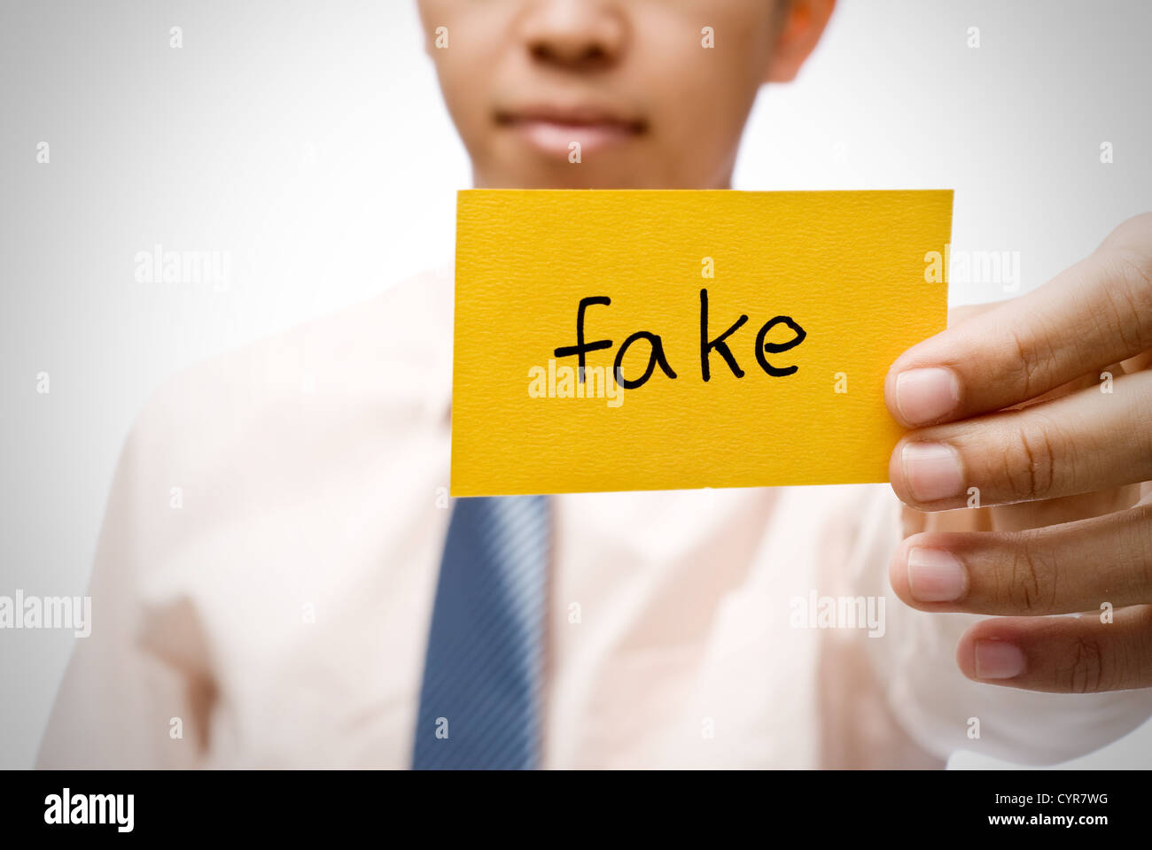 Fake word on yellow card holding by businessman Stock Photo - Alamy