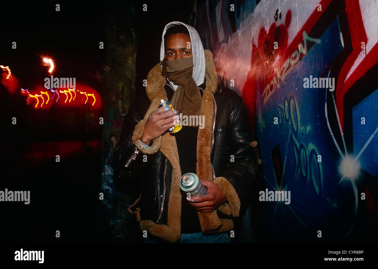 A masked youth is seen after spraying graffiti art on to a wall in the ...