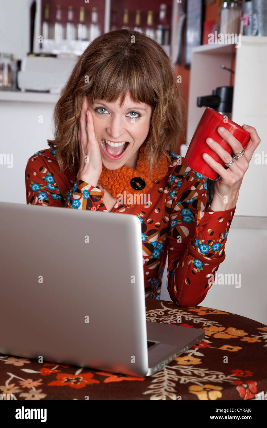 Blushing brunette with laptop holding red mug at a cafe Stock Photo - Alamy