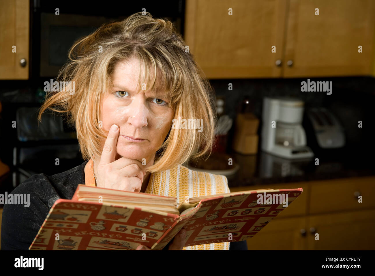 Harried woman in residential kitchen with recipe book Stock Photo - Alamy
