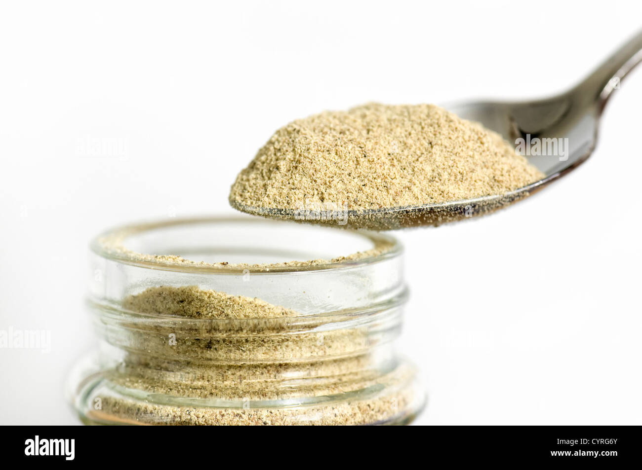Close up of a spoonful of ground white pepper against a white ...