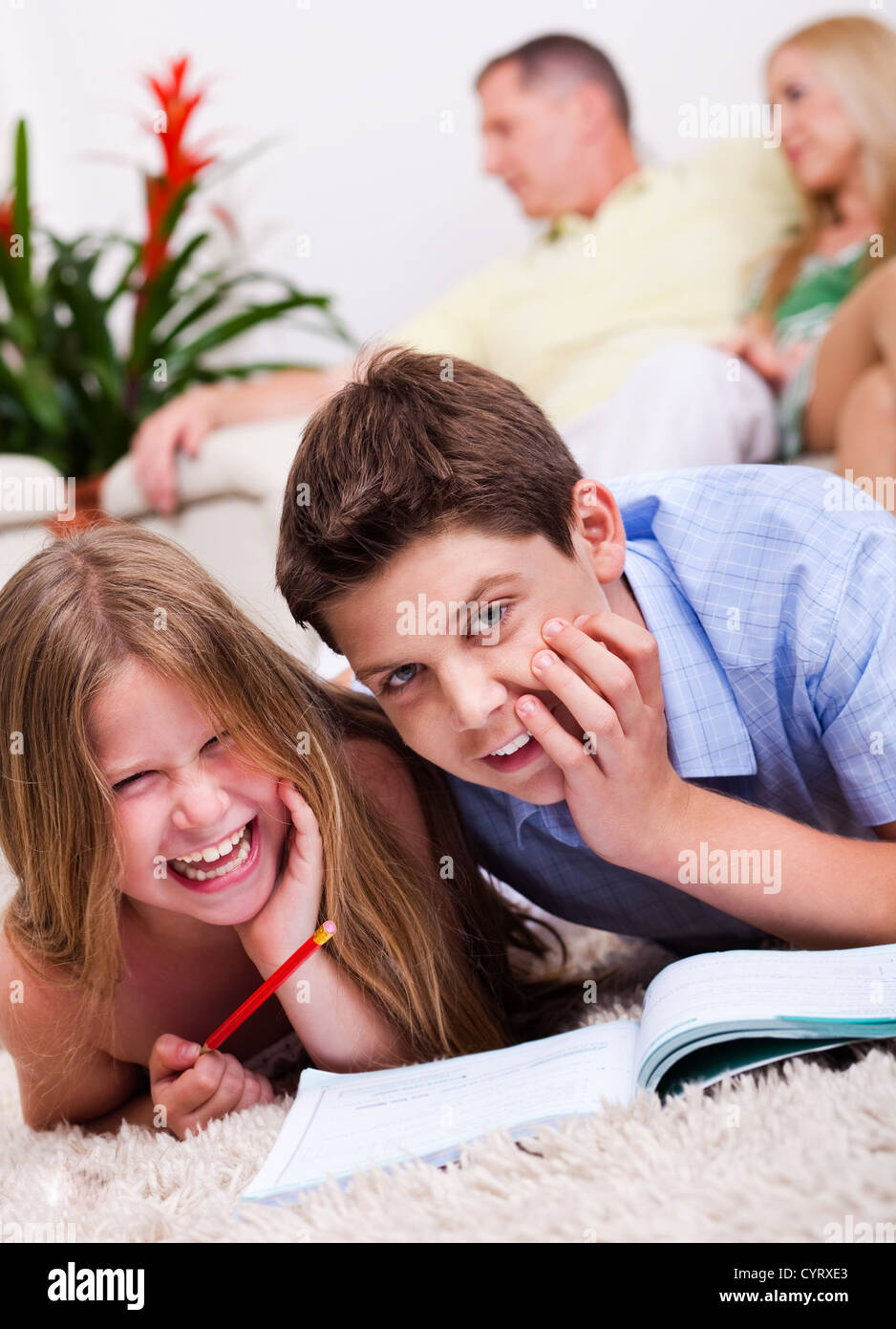 Two young kids lying with a book in living room and their parents on ...