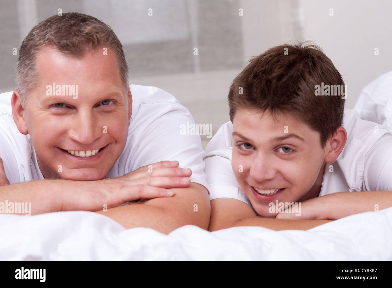 Friendly father and son smiling and lying on the bed and looking at you ...