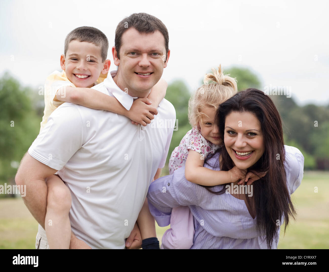 Smiling couple carrying kids on their back over natural background ...