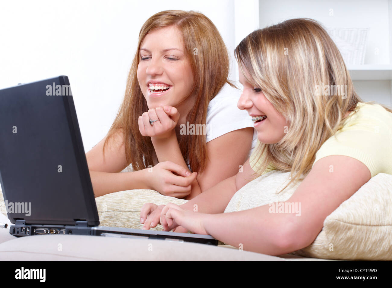 Two girls laying on the sofa with laptop computer one has got a brace ...