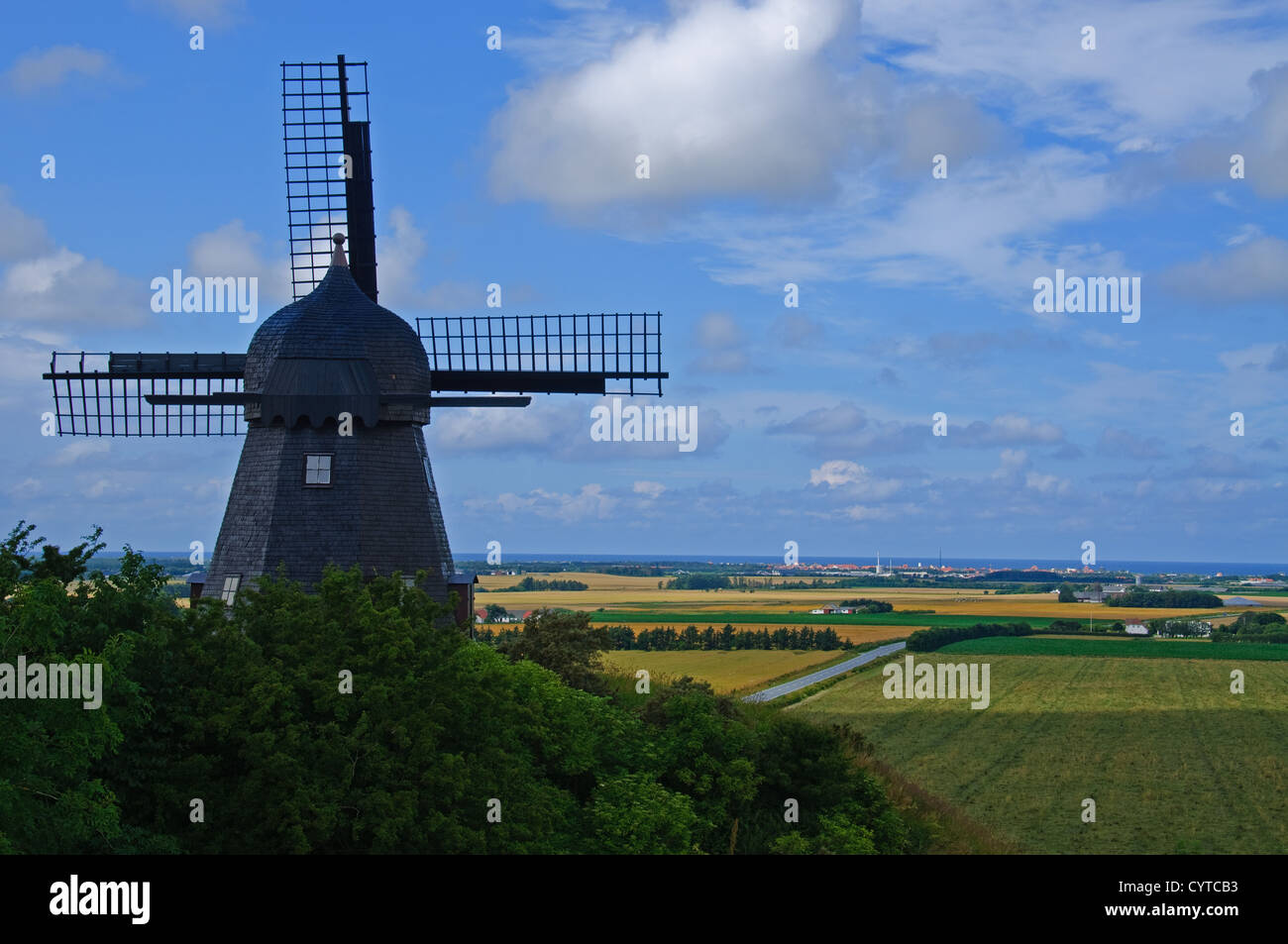 An old dark windmill on a hill with a view over fields and to the ocean ...