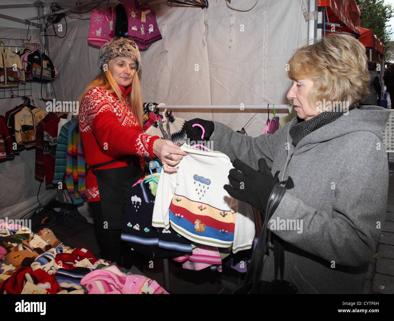 Female stall holder selling child's knitted coat to customer, York open ...
